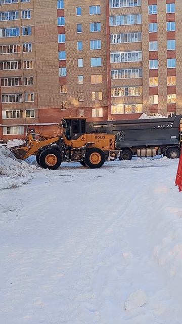 Трактор складывает снег в самосвал