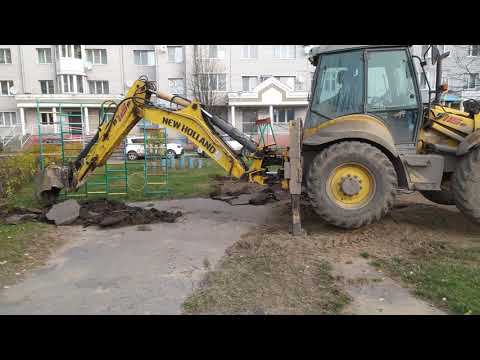 Экскаватор-погрузчик New Holland ломает асфальт.